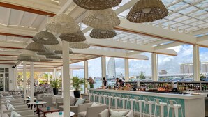 Uma área de bar ampla com vista para o mar e barcos, rodeada por assentos confortáveis e um bar bem abastecido.