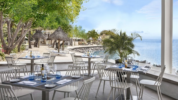 Restaurante à beira-mar com área externa, mesas preparadas com copos azuis e vista para o oceano.