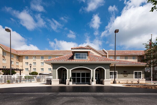 Entrada de hotel com telhado telhado, arco de entrada e placa com a inscrição 'Homewood Suites Hilton'.