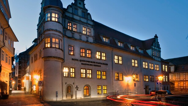 Um edifício histórico com várias janelas e uma torre imponente, identificado como Hotel Quedlinburger Stadtschloss.