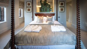 Uma grande cama de dossel com cabeceira de madeira, lençóis brancos e duas toalhas dobradas sobre a cama.