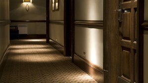 Um corredor com carpete estampado, portas de madeira e luminária fixada na parede.