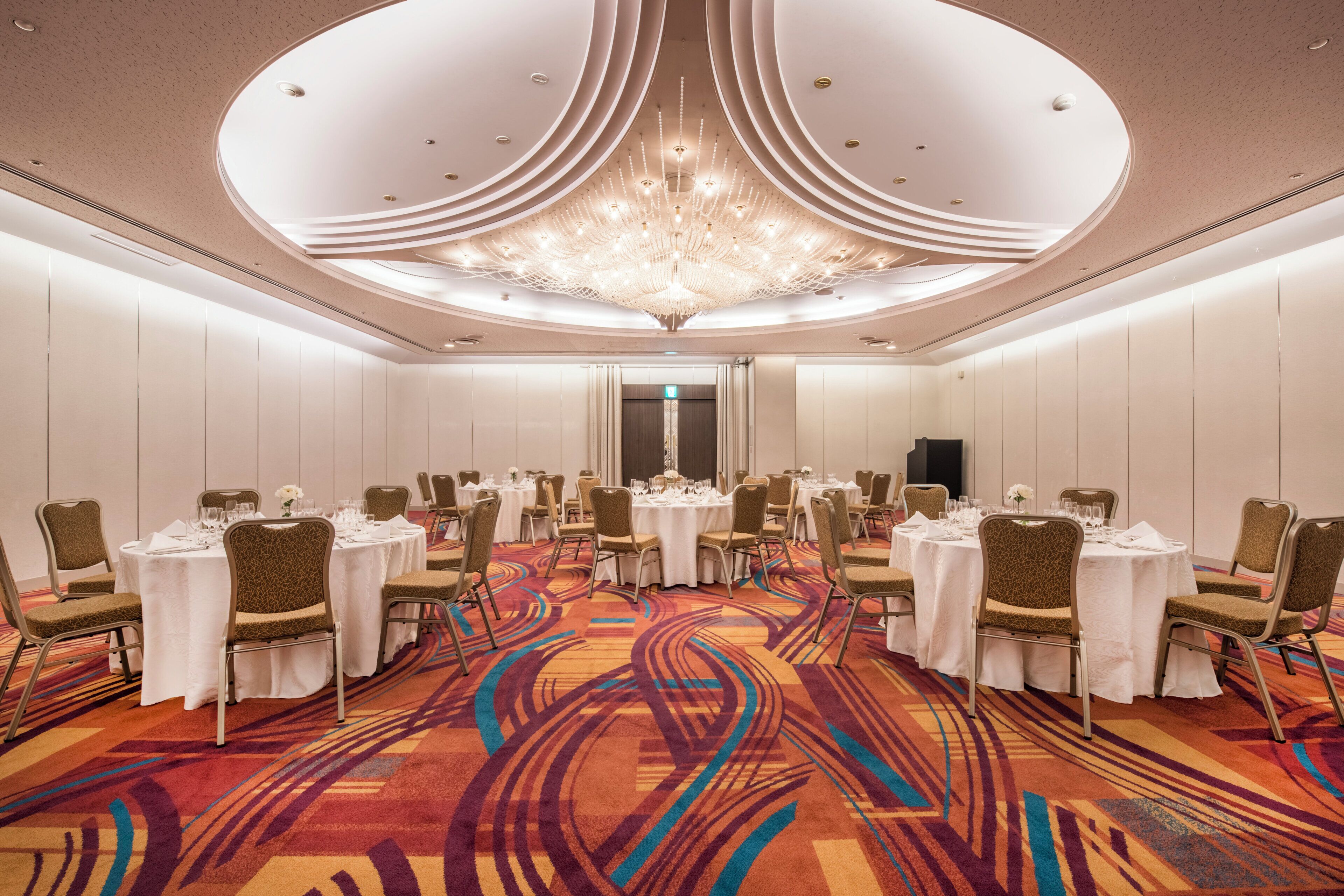 Sala de conferências com mesas redondas, cadeiras e um lustre grande.