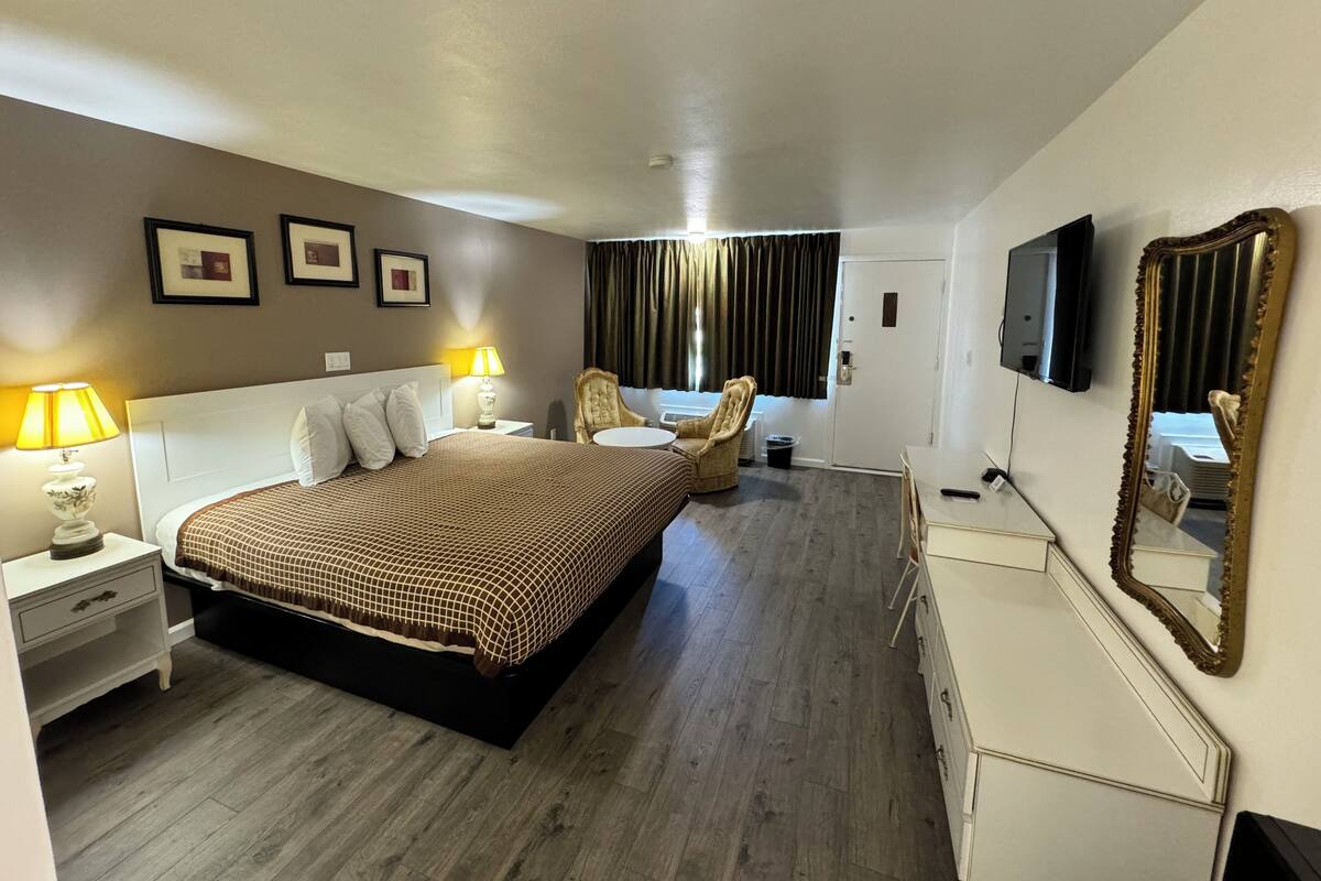 Quarto de hotel com uma cama grande, duas mesas de cabeceira, uma cadeira, uma escrivaninha, uma televisão e um espelho.