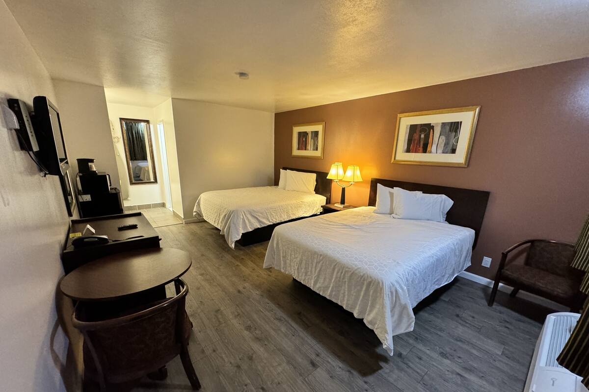 Quarto de hotel com duas camas, uma escrivaninha, uma cadeira e uma televisão.