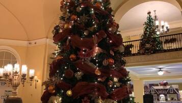 Uma grande árvore de Natal decorada no saguão de um hotel, com teto alto e janelas em arco.
