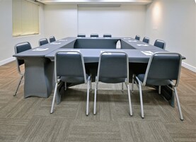 Uma sala de conferências com uma grande mesa retangular, seis cadeiras e uma tela de projetor.