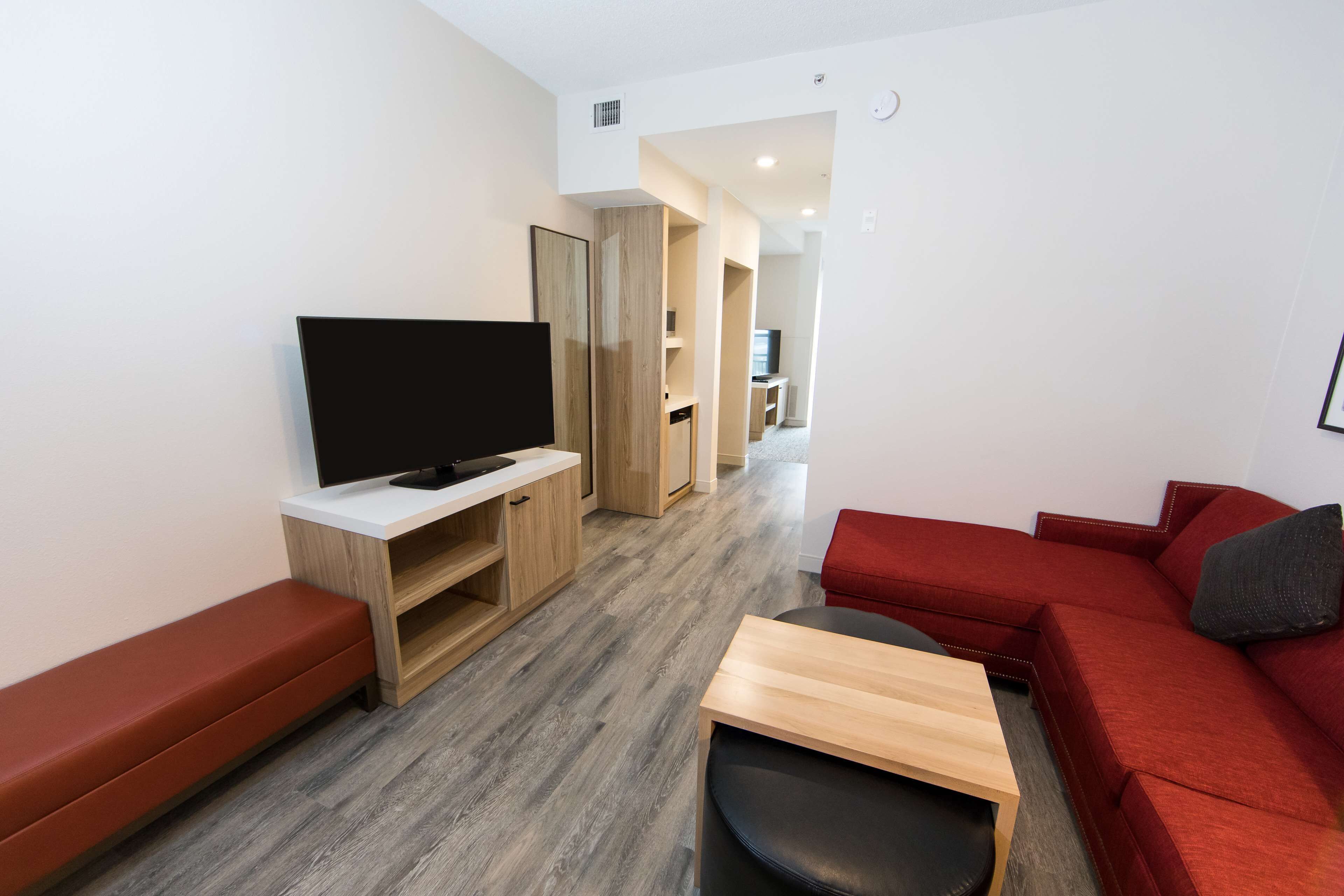Uma sala de estar moderna com um sofá vermelho, uma mesa de centro de madeira, uma TV sobre um móvel e um banco.