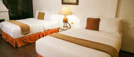 Quarto de hotel com duas camas, uma mesa de cabeceira com luminária e um quadro na parede.