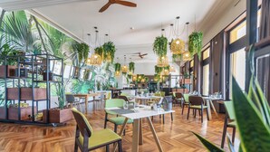 Um restaurante amplo com piso de madeira, cadeiras verdes e plantas pendentes.
