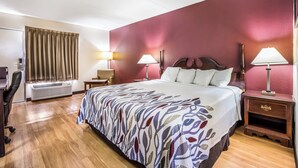 Quarto de hotel com uma cama grande, duas luminárias de cabeceira, uma escrivaninha e um ar condicionado.