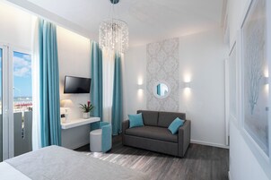 Quarto moderno com sofá cinza, televisão, mesa de cabeceira e janela com cortinas.
