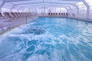 Piscina interior com água cristalina, um trampolim e espreguiçadeiras.