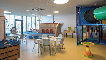 Espaço de recreação infantil com mesas, cadeiras e um parquinho.