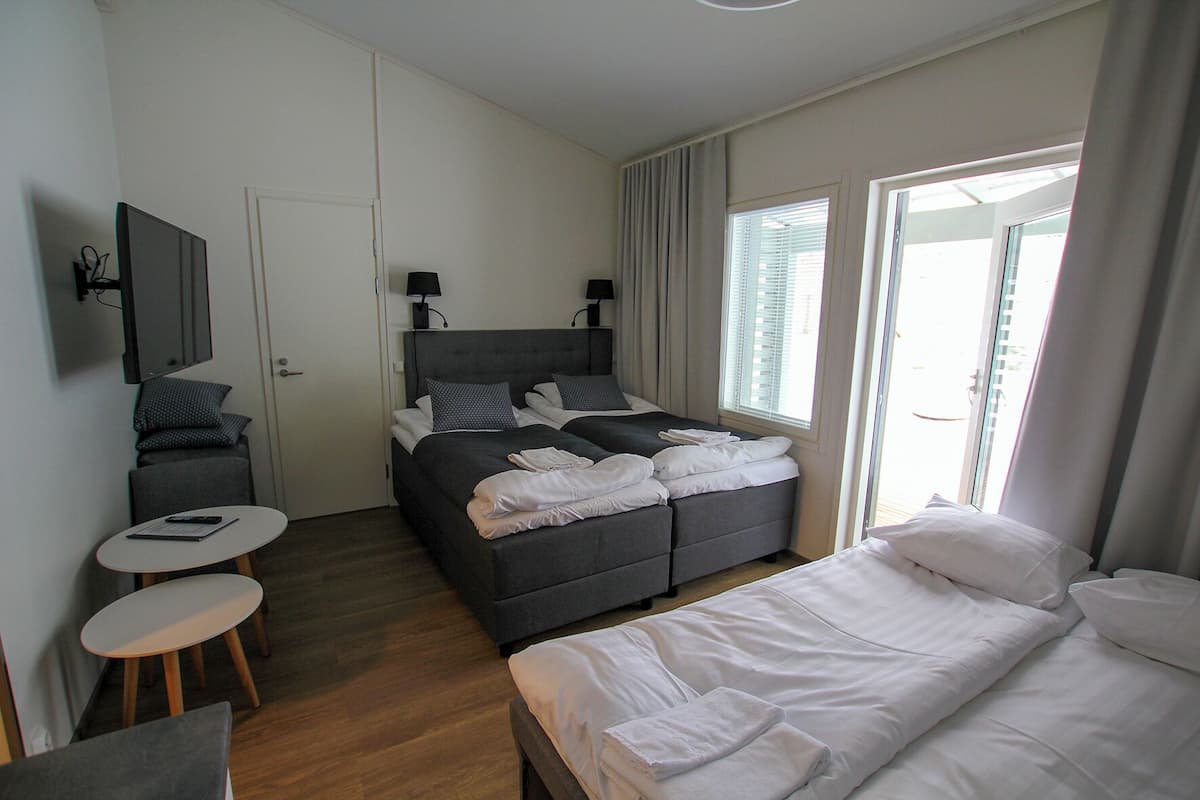 Quarto de hotel com uma cama grande, uma cama menor, uma escrivaninha e uma cadeira.