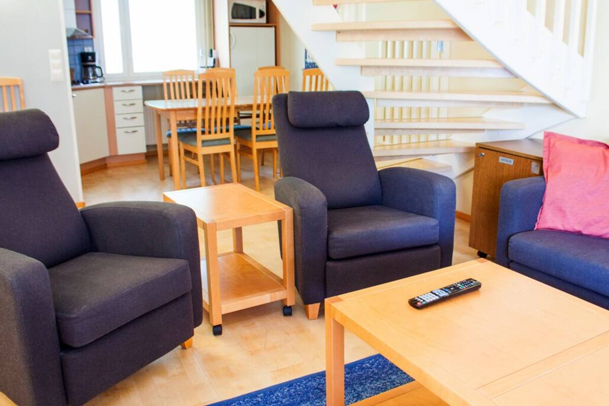 Uma sala de estar moderna com sofás escuros, uma mesa de centro de madeira e um sofá azul com uma almofada rosa. Um controle remoto está sobre a mesa.