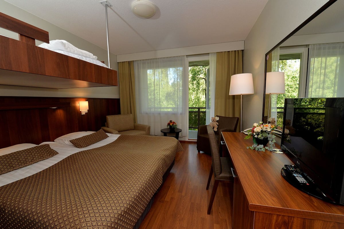 Quarto de hotel com uma cama grande, uma escrivaninha com televisão, uma cadeira e uma janela com vista para áreas verdes.