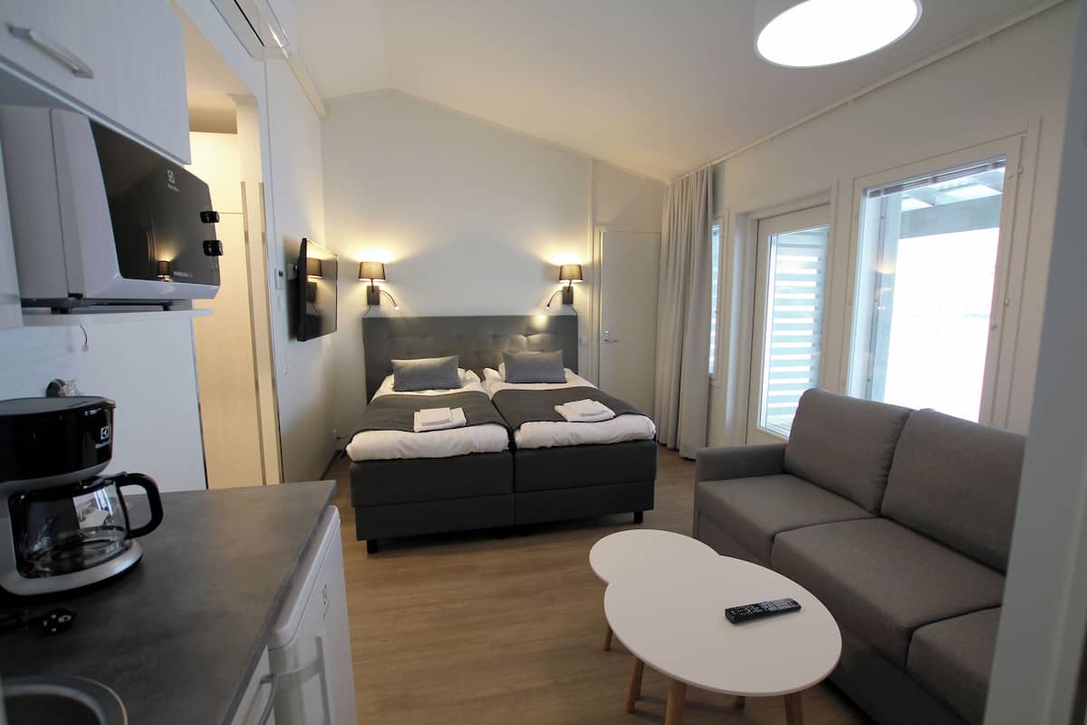 Quarto de hotel moderno com cama, sofá, máquina de café e televisão.