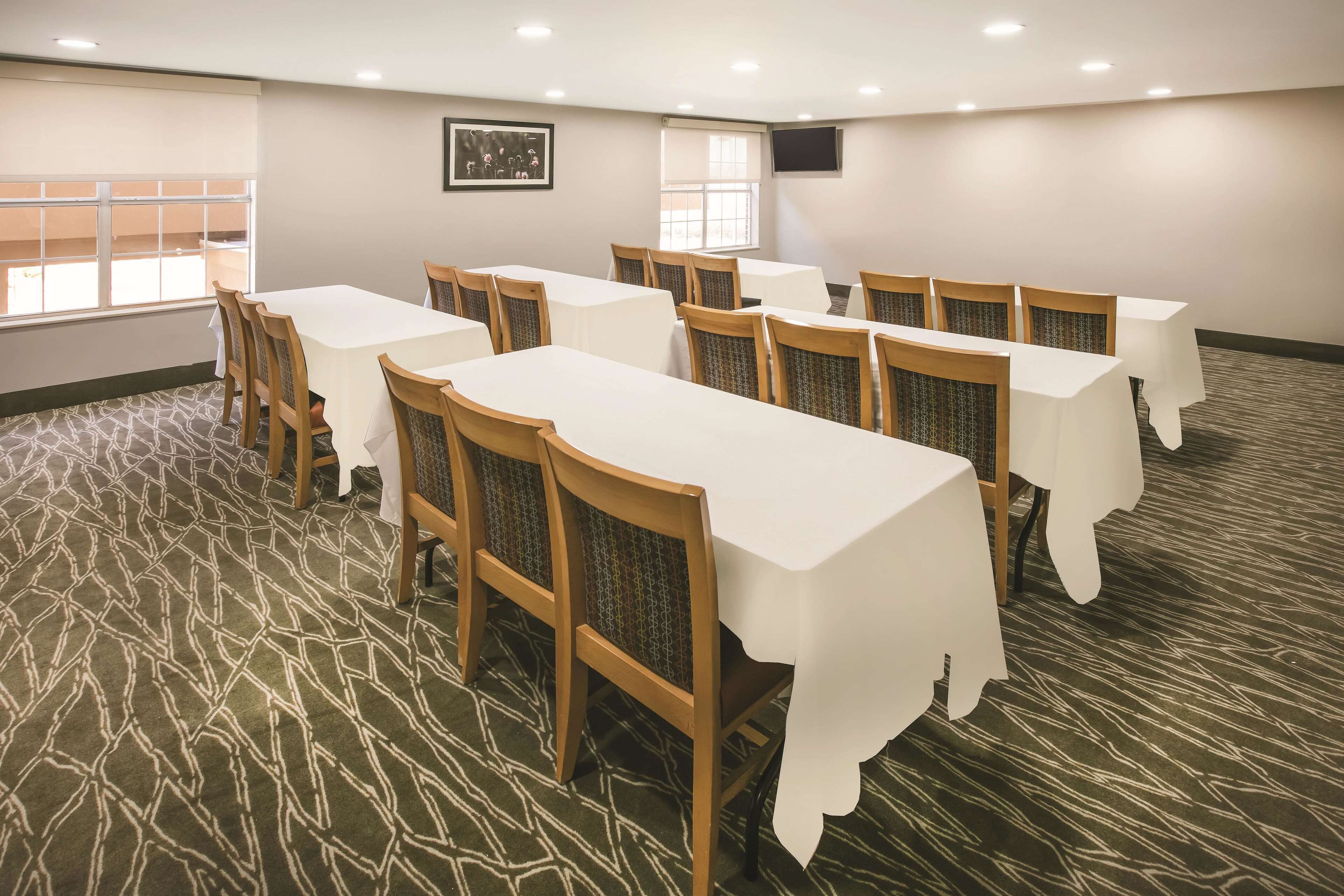 Sala de conferências com várias mesas e cadeiras, piso coberto de carpete e uma janela grande.