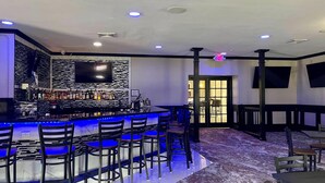 Uma área de bar com balcão, vários bancos e uma televisão fixada na parede.
