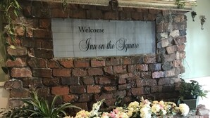 Paredes de tijolo com uma placa de boas-vindas, plantas em vasos e um arranjo floral.