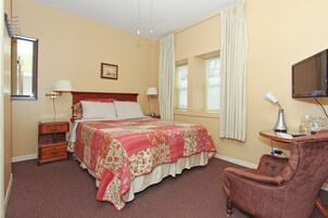 Quarto de hotel com uma cama grande, duas mesas de cabeceira com luminárias, uma televisão e uma cadeira.