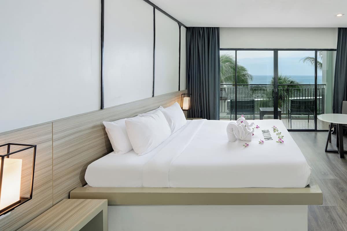 Quarto de hotel com uma cama grande, uma mesa de trabalho, uma cadeira, uma televisão e varanda com vista para o oceano.
