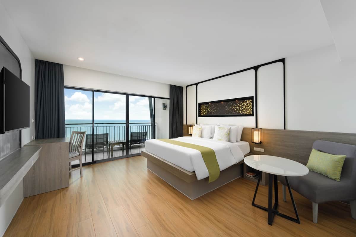 Quarto de hotel moderno com uma cama grande, área de estar, varanda com vista para o mar e televisão de tela plana.