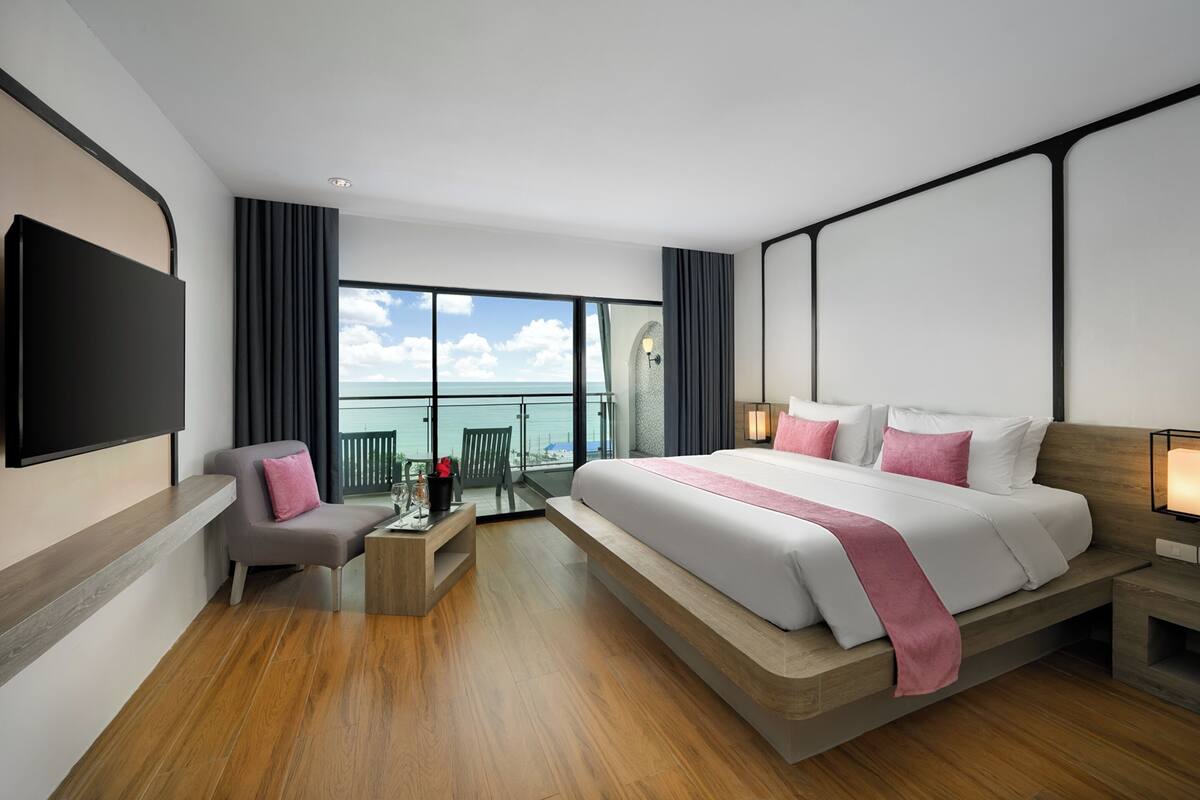 Quarto de hotel moderno com uma cama grande, área de estar e varanda com vista para o mar.