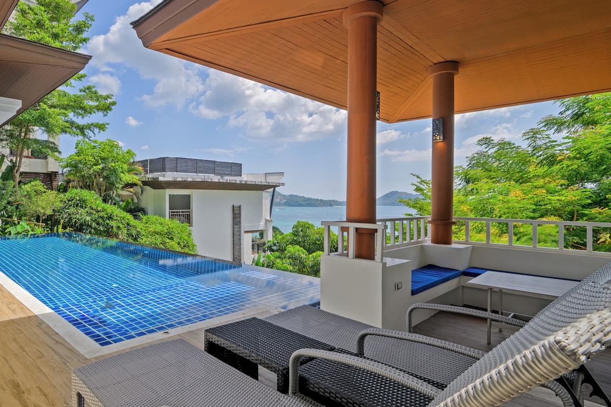 Piscina infinita no terraço, com vista para o mar, rodeada por espreguiçadeiras e uma área de estar coberta.