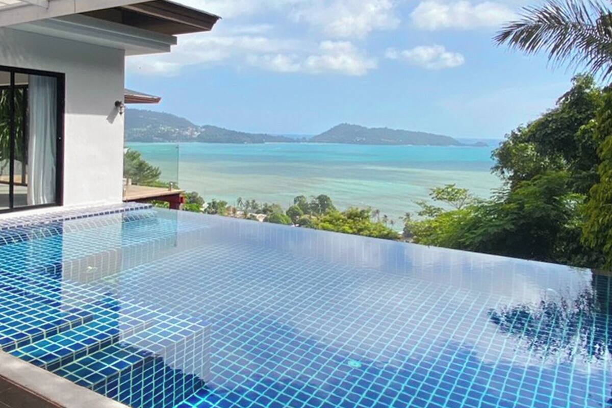 Uma piscina infinita moderna com vista clara do oceano e montanhas ao longe.