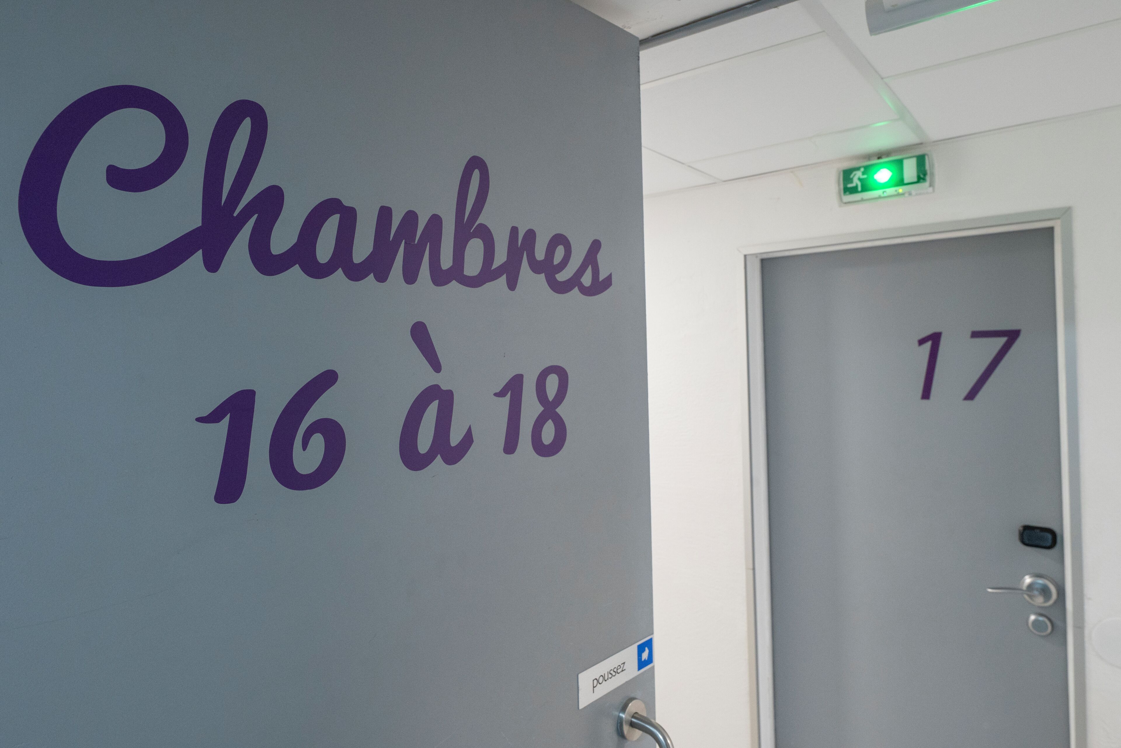 Quarto de hotel com uma placa na parede indicando 'Chambres 16 à 18' e uma porta com a inscrição '17'.