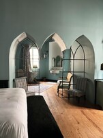 Quarto com uma cama grande, duas cadeiras, piso de madeira e uma janela com cortinas.