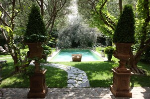 Um jardim com um caminho de pedra que leva a uma piscina, rodeado por vegetação exuberante e árvores.