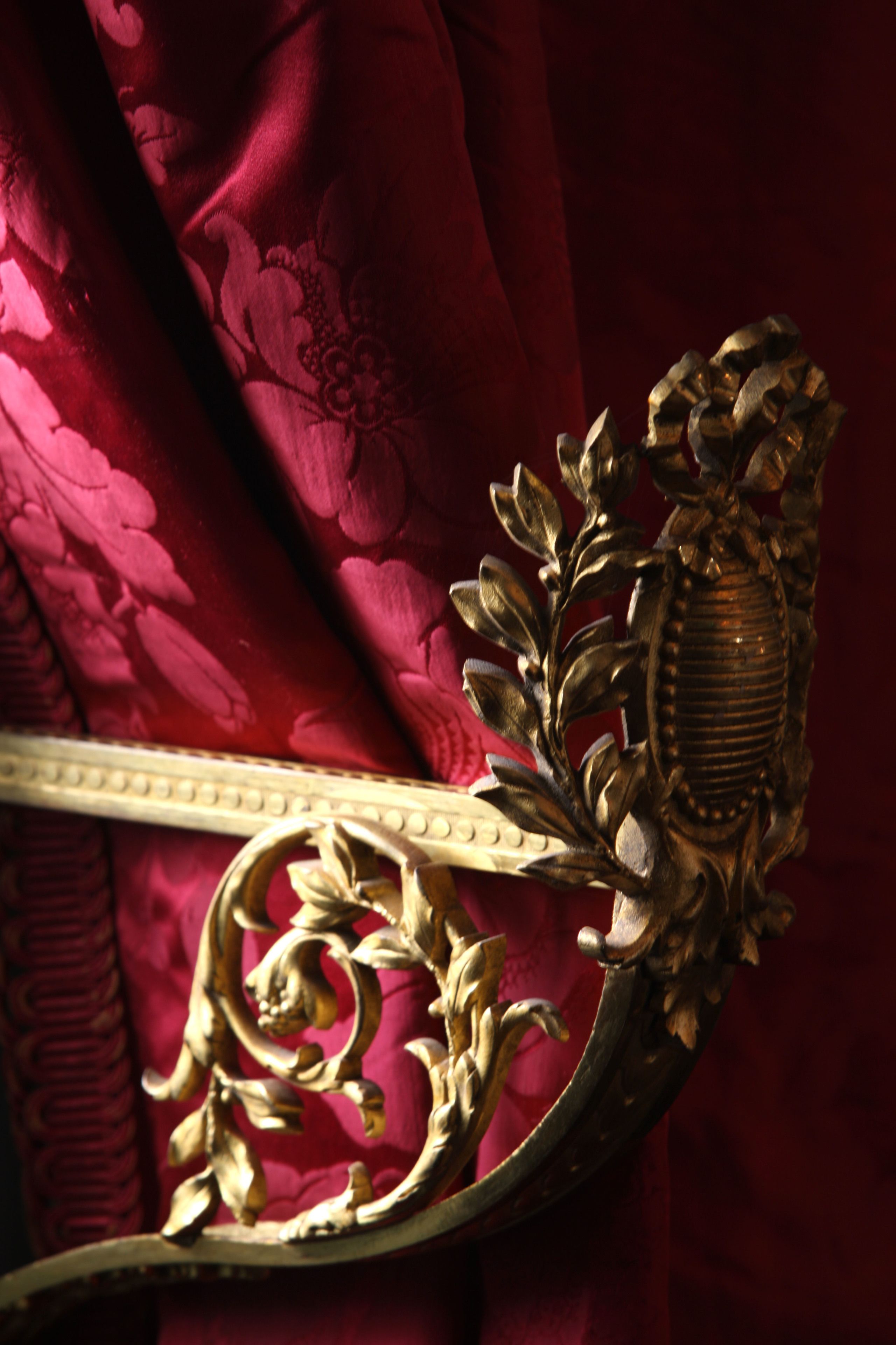 Close-up de uma espada dourada ornamentada com uma empunhadura detalhada, sobre um fundo de tecido vermelho.