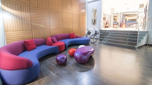 Um interior moderno com um sofá curvo azul e vermelho, uma bicicleta e uma escada que leva a uma área iluminada.