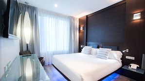 Quarto de hotel moderno com uma cama grande, uma mesa de vidro, televisão e telefone ao lado da cama.