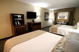 Quarto de hotel com duas camas, televisão, escrivaninha com cafeteira e janela com cortinas.