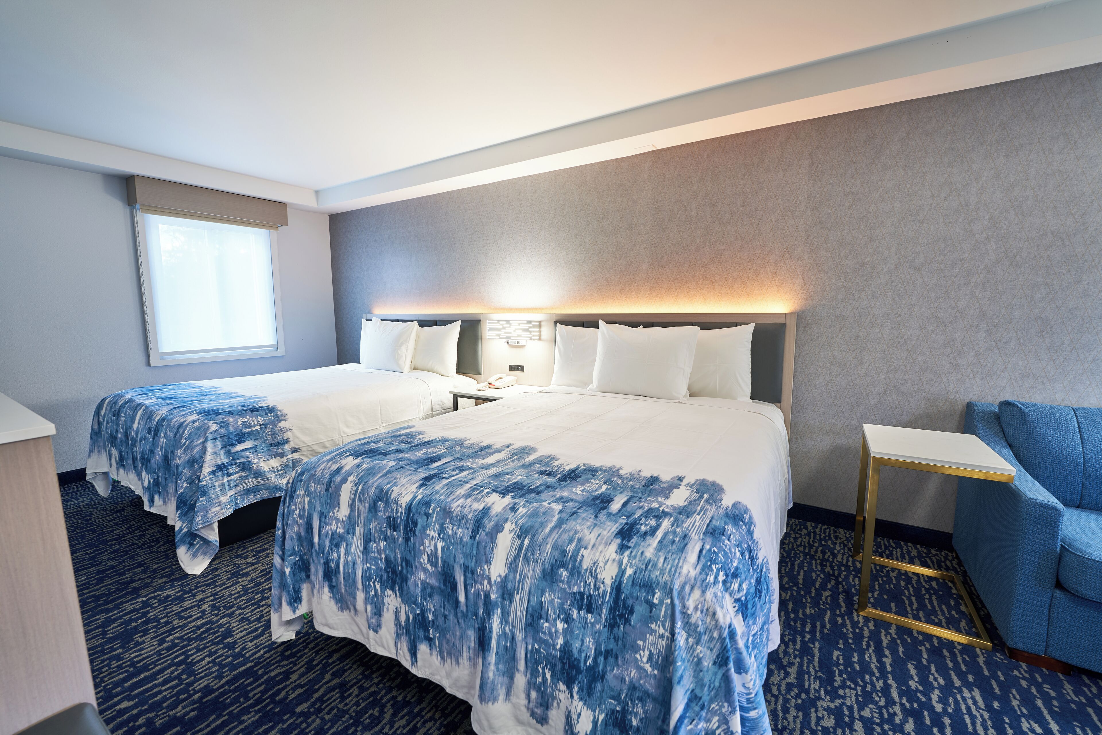 Quarto de hotel com duas camas, uma escrivaninha, uma cadeira e uma janela.