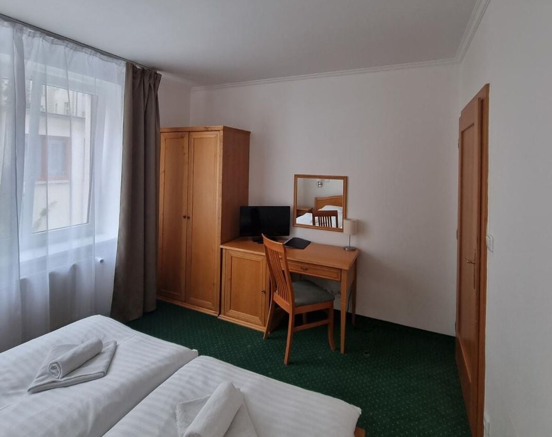 Quarto de hotel com cama, escrivaninha, cadeira, guarda-roupa e espelho.