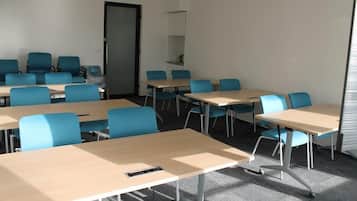 Sala de conferências com várias mesas e cadeiras azuis, uma porta e uma janela.