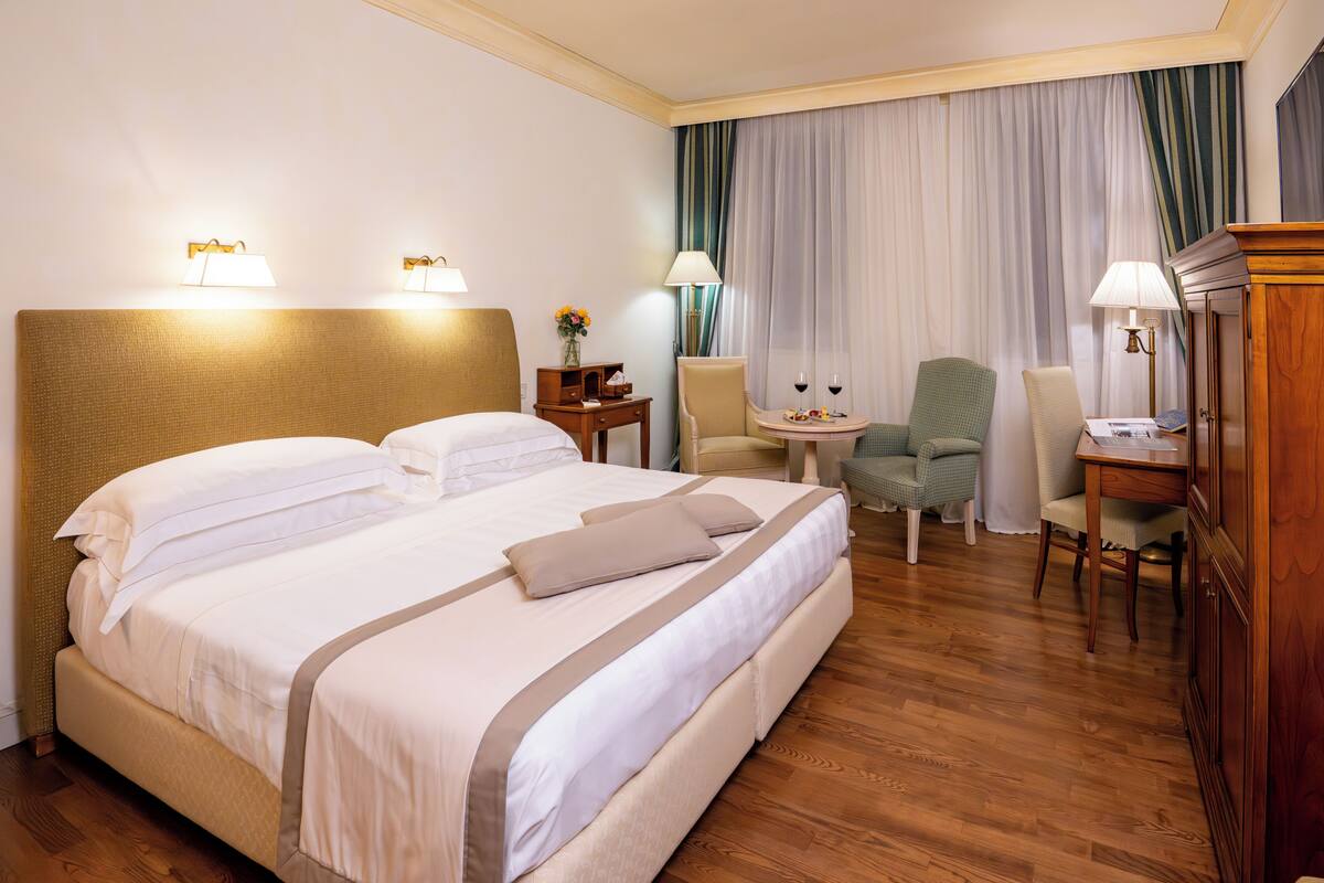 Quarto de hotel com uma cama grande, duas mesas de cabeceira, uma escrivaninha e uma cadeira.