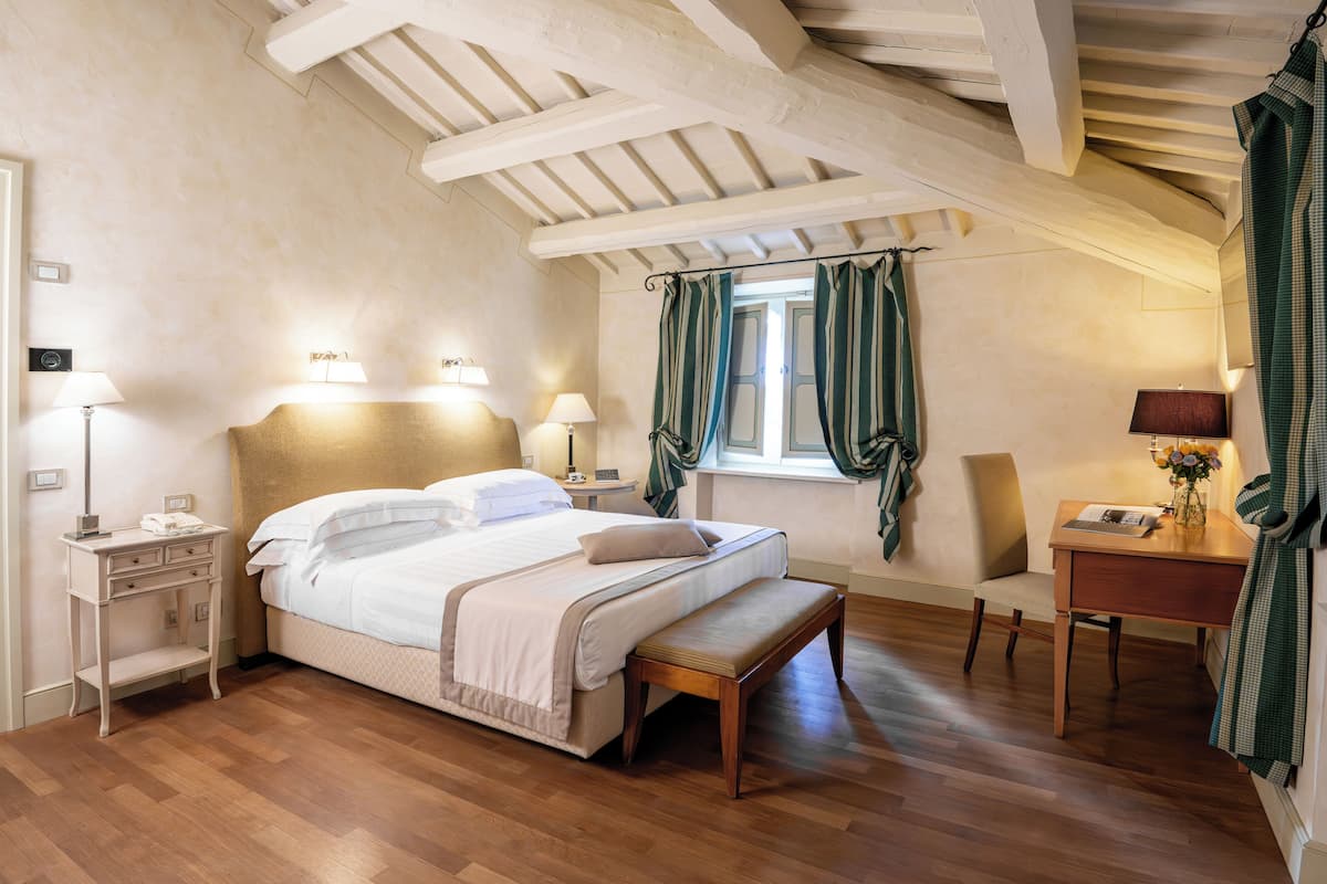 Um quarto com cama de madeira, mesas de cabeceira, escrivaninha e janela com cortinas.
