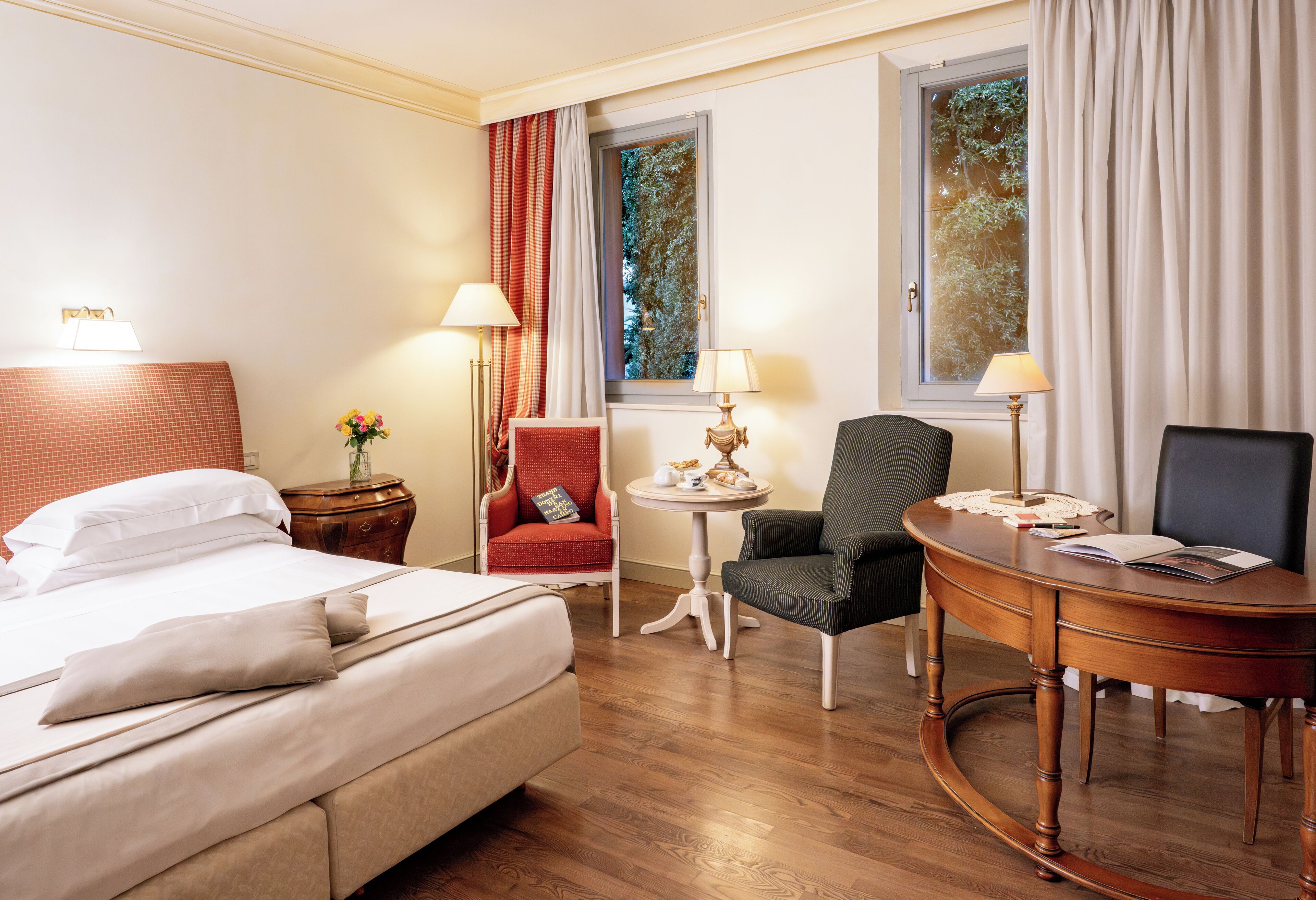 Quarto de hotel com cama, escrivaninha, cadeira e mesa pequena.