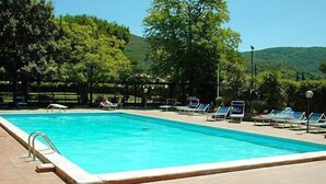 Piscina retangular com deck revestido, cercada por cadeiras de descanso e um cercado.
