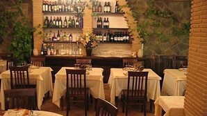 Interior de restaurante com várias mesas, cadeiras e um bar com garrafas de vinho.
