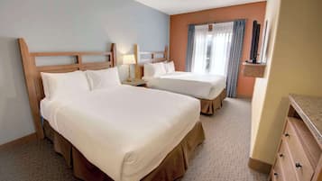 Quarto de hotel com duas camas, um ventilador de teto, uma janela com cortinas e uma cômoda de madeira.