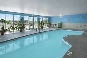 Piscina com água azul cristalina, rodeada por plantas em vasos e área de estar externa.