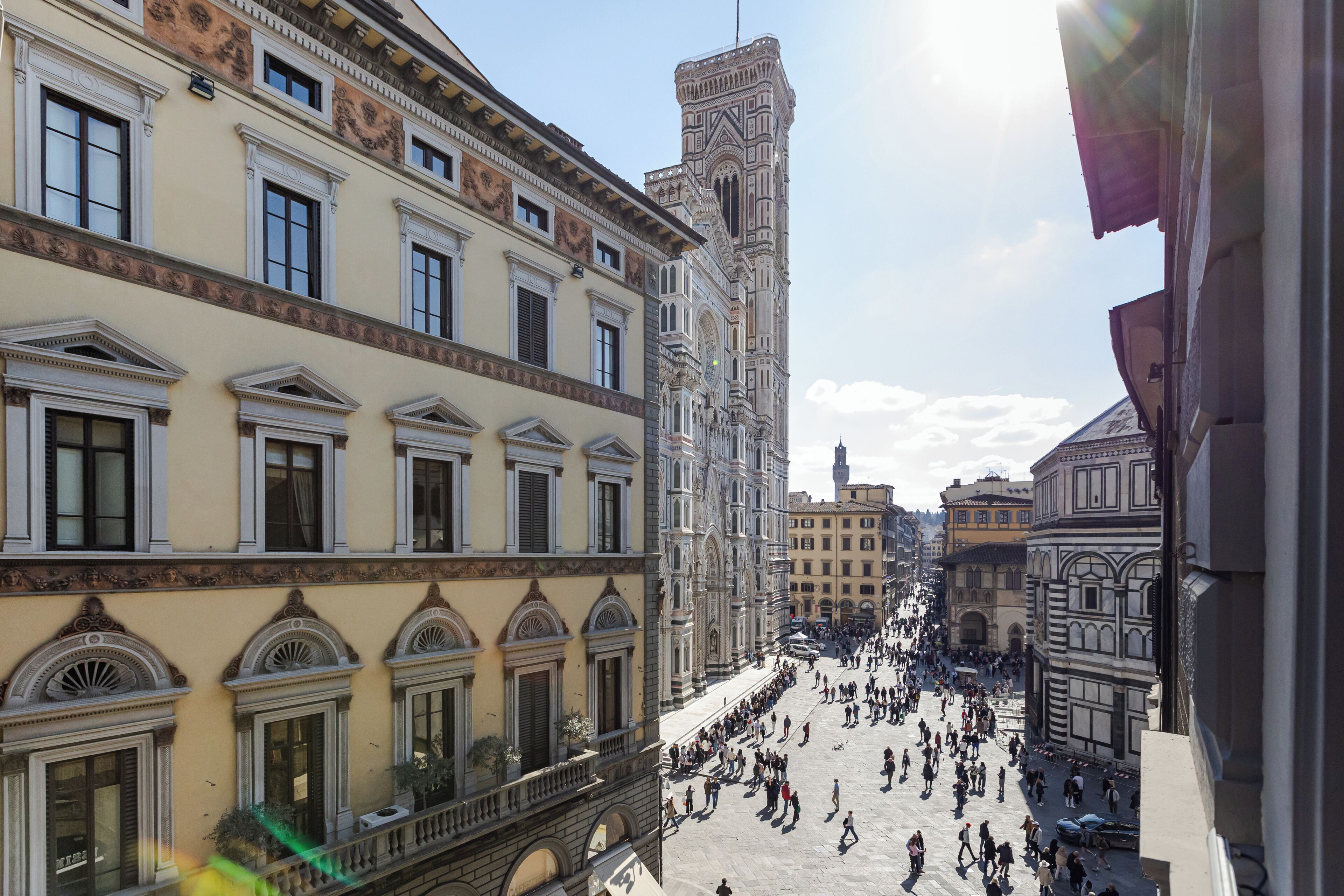 Uma praça histórica com arquitetura clássica, incluindo fachadas ornamentadas e uma torre imponente.