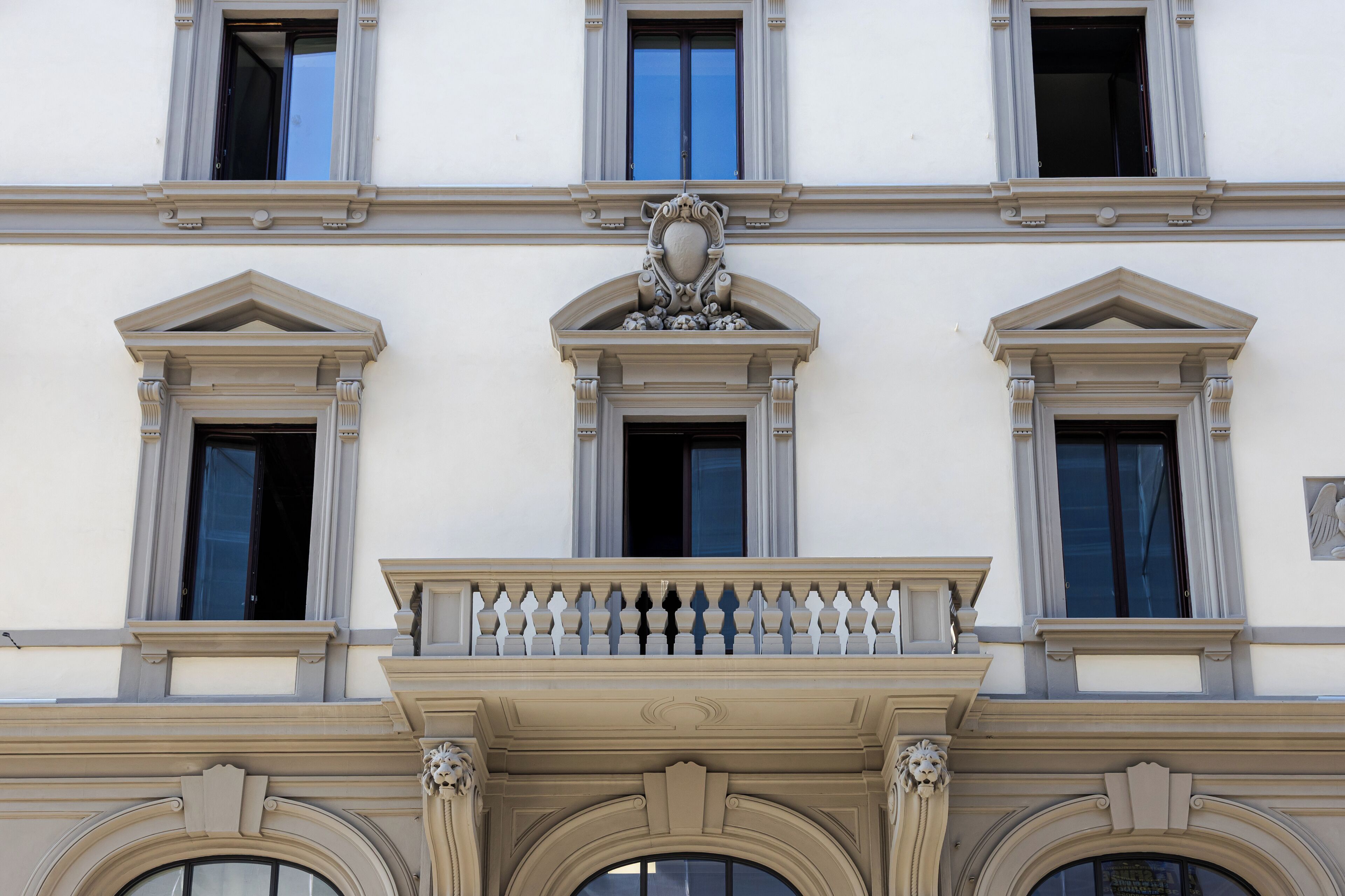 Fachada de edifício com três janelas, um elemento decorativo central e um corrimão.
